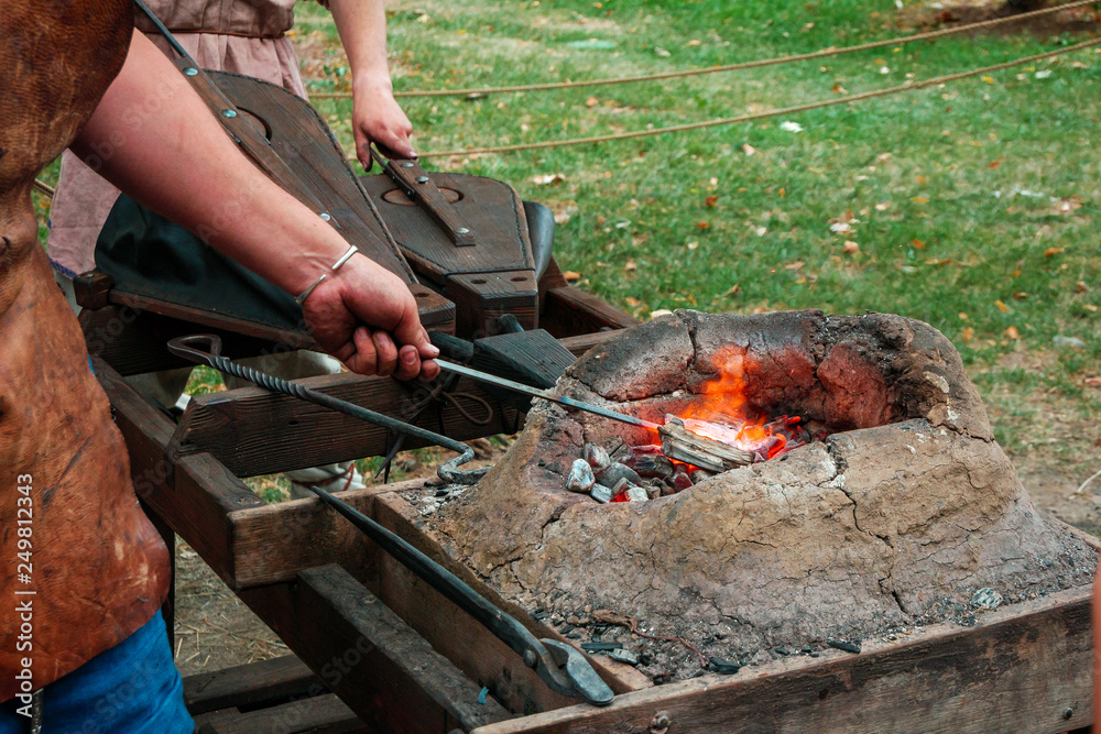 Blacksmiths in ancient clothes poking burning coals in medieval furnace ...