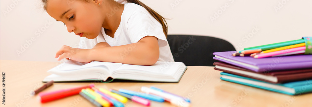 Cute little girl doing homework, reading a book, coloring pages ...
