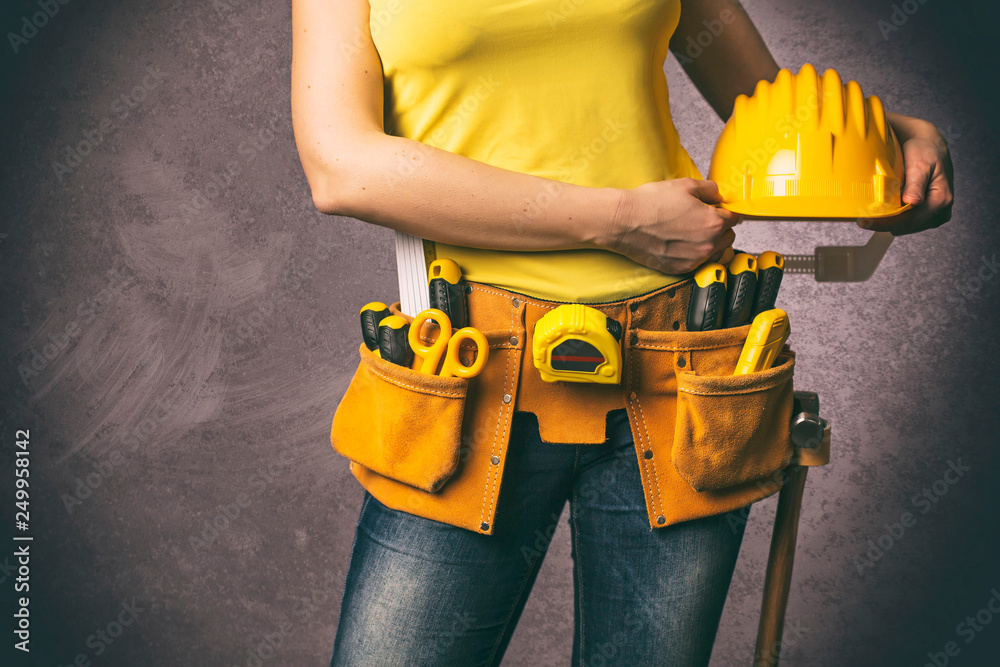 Handywoman with helmet and tool belt on concrete background. Stock ...