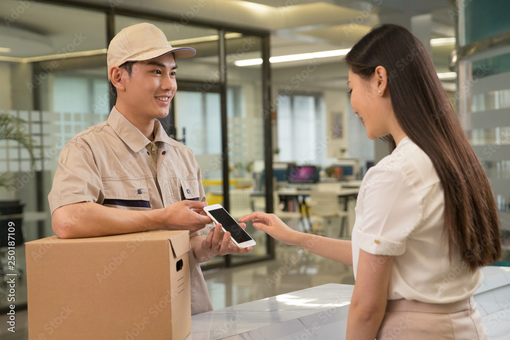 Delivery man showing smartphone to woman at reception Stock Photo ...