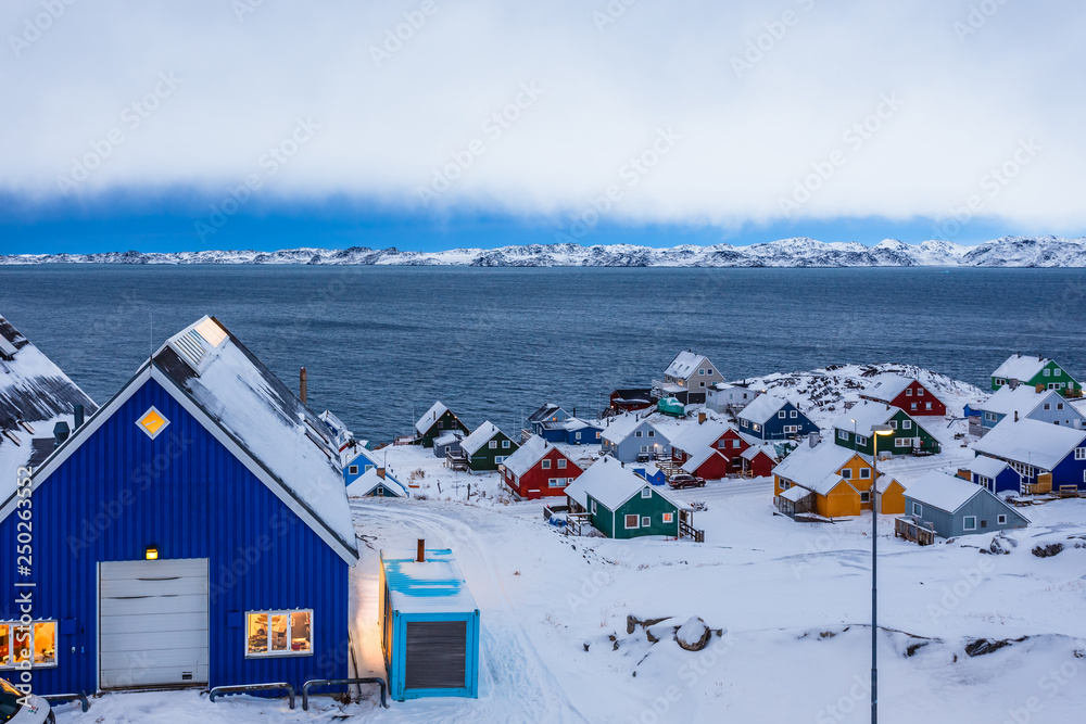 Colorful inuit huts among rocks and snow at the fjord in a suburb of ...