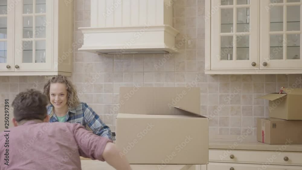 Cheerful man and woman running after each other in the kitchen, man ...