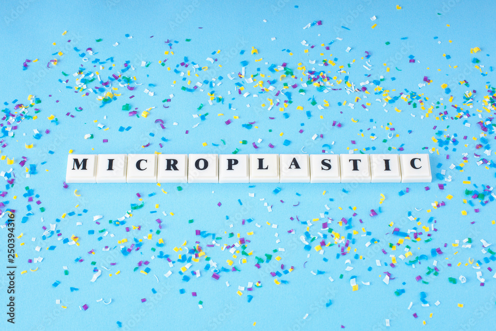 Word MICROPLASTIC around small plastic particles on a blue background ...
