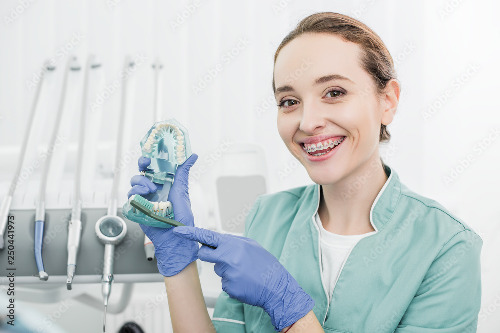 beautiful dentist with braces on teeth holding teeth model and showing ...