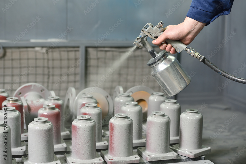 A worker at a factory in a special room paints parts of the valves from ...