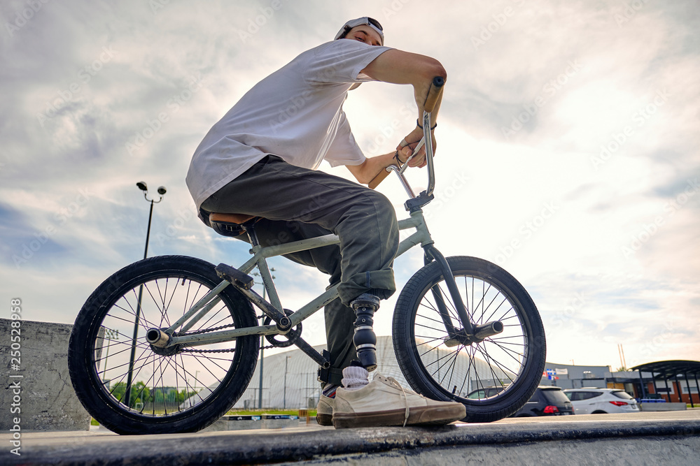 BMX rider with prosthetic foot confidently posing on bike against ...