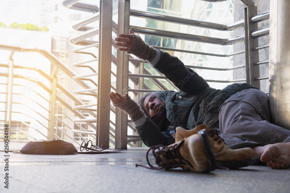 Homeless man is lie down on walkway in town. He is raise hand for ...