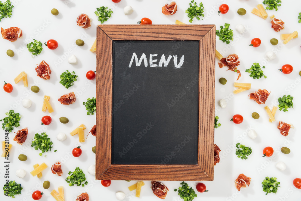 chalk board with menu lettering among olives, prosciutto, greenery ...