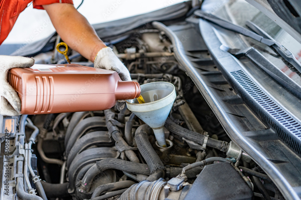 Car mechanic replacing and pouring fresh oil into engine at maintenance ...