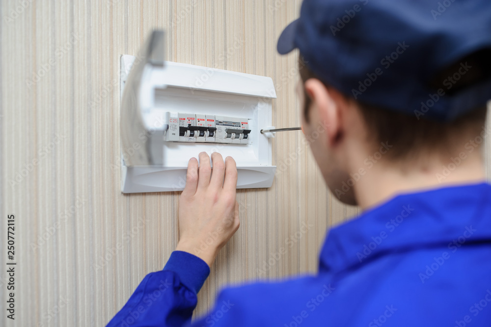 lateral view of a young eletrician in blue overall disassembling a ...