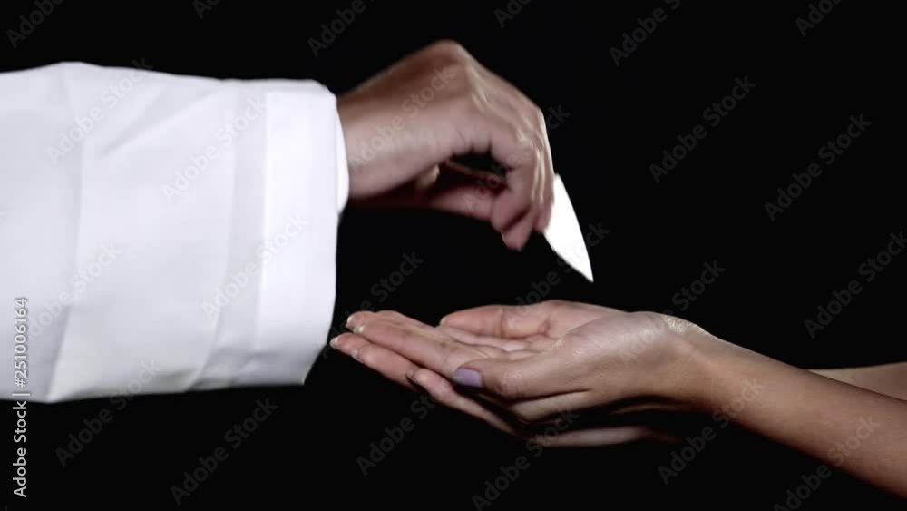 Priest giving first communion bread on woman hands over dark background ...