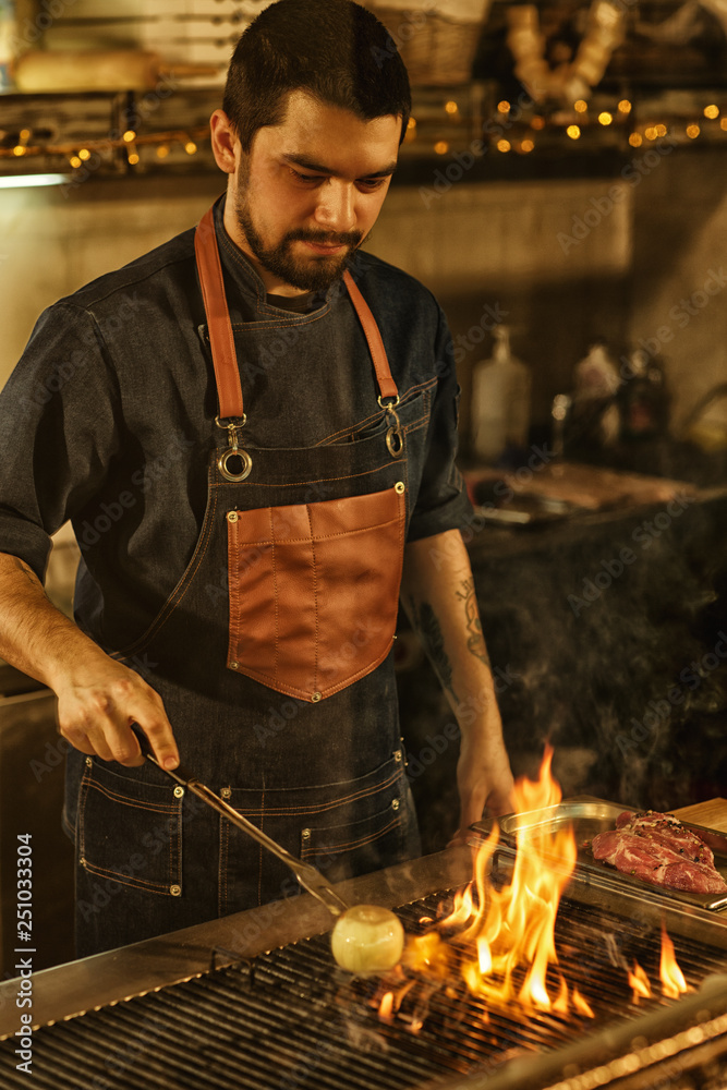 Professional chef cooking onion, vegetables and meat on grill with fire ...