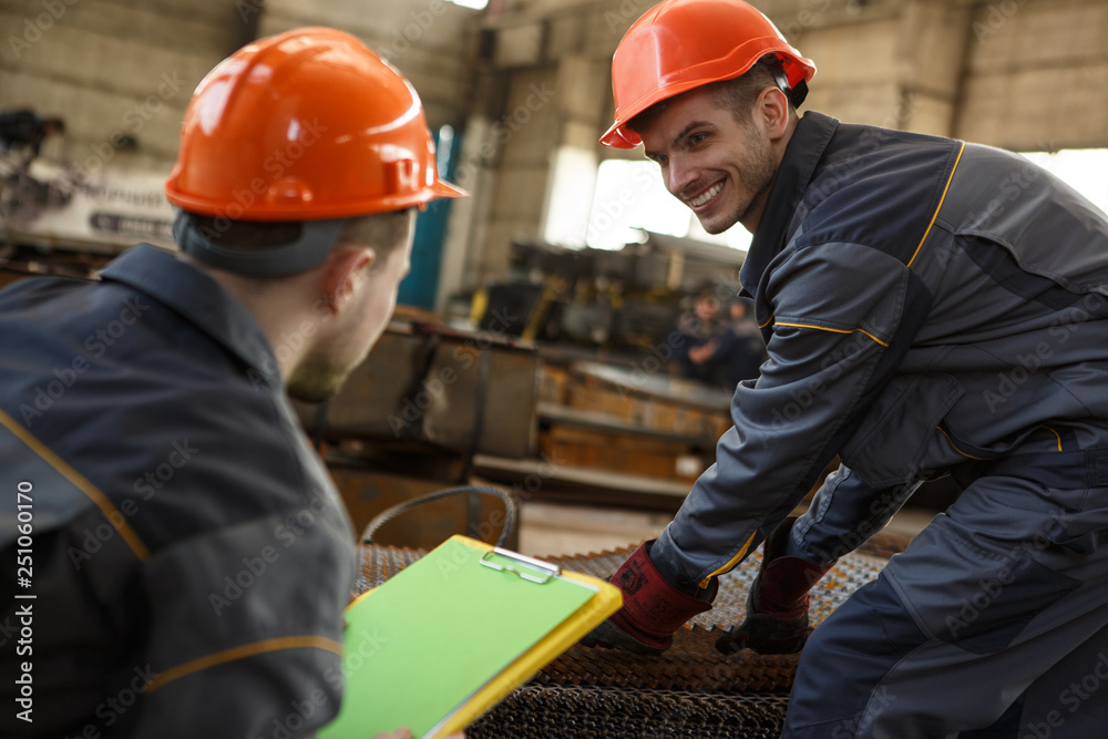 Side view of two workers of metal stock in uniform, orange helmets and ...