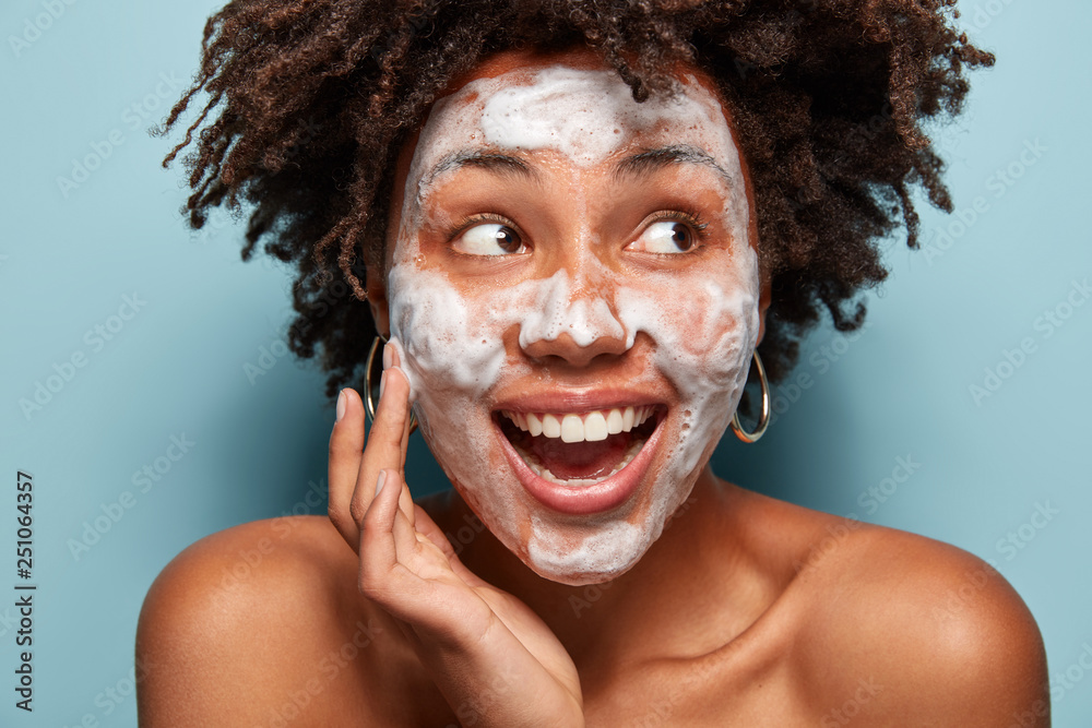 Headshot of happy black woman with foam or foaming cleanser on face ...