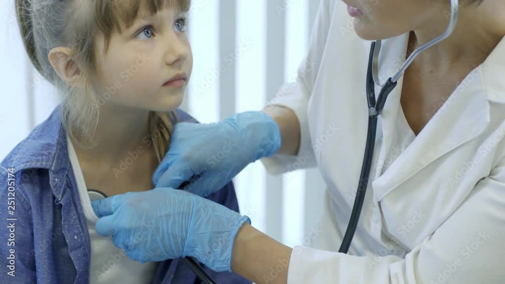 Kind female doctor listening to lung sound of cute little girl with ...