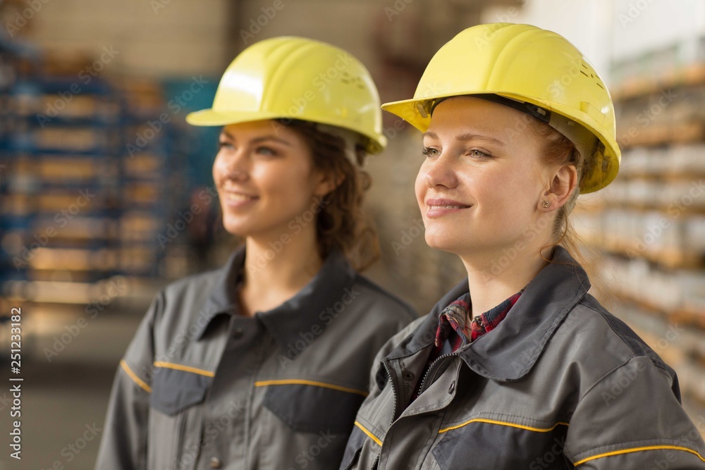 Portrait of two female workers wearing in uniforms and yellow helmets ...