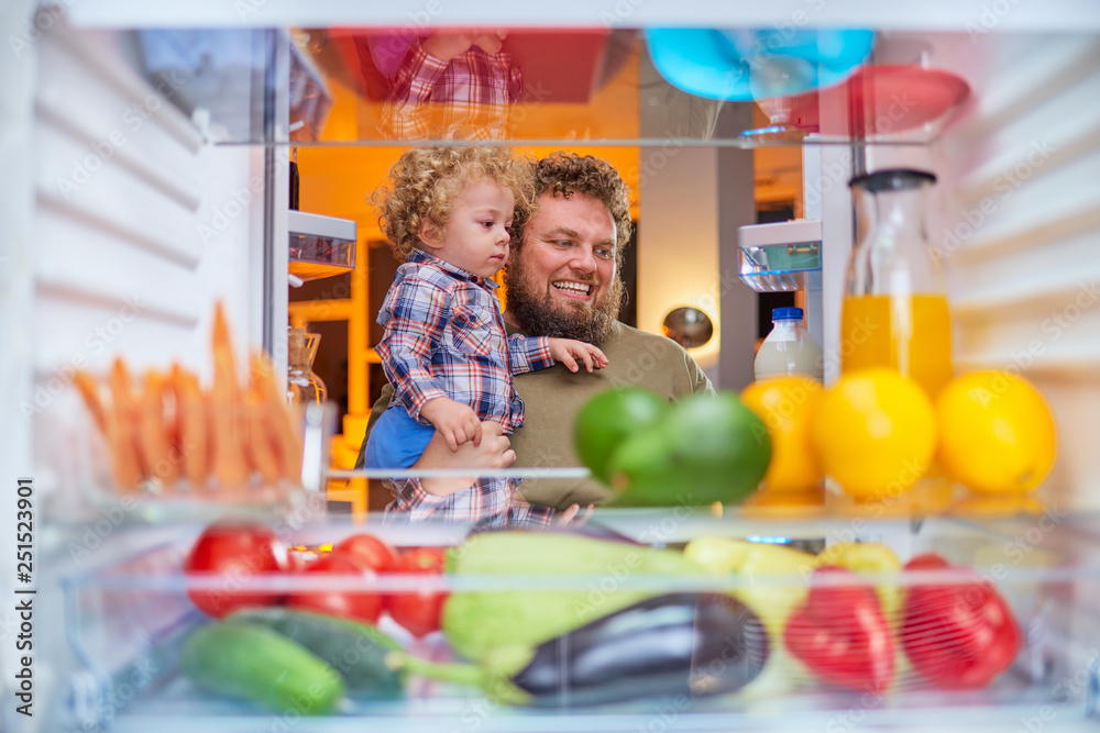 Father and son standing in front of opened fridge and looking something ...