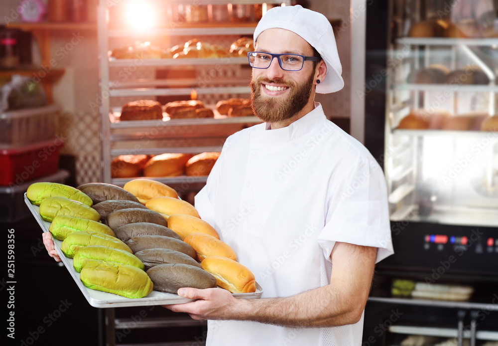 young cute Baker in white uniform holding a tray with colored rolls for ...
