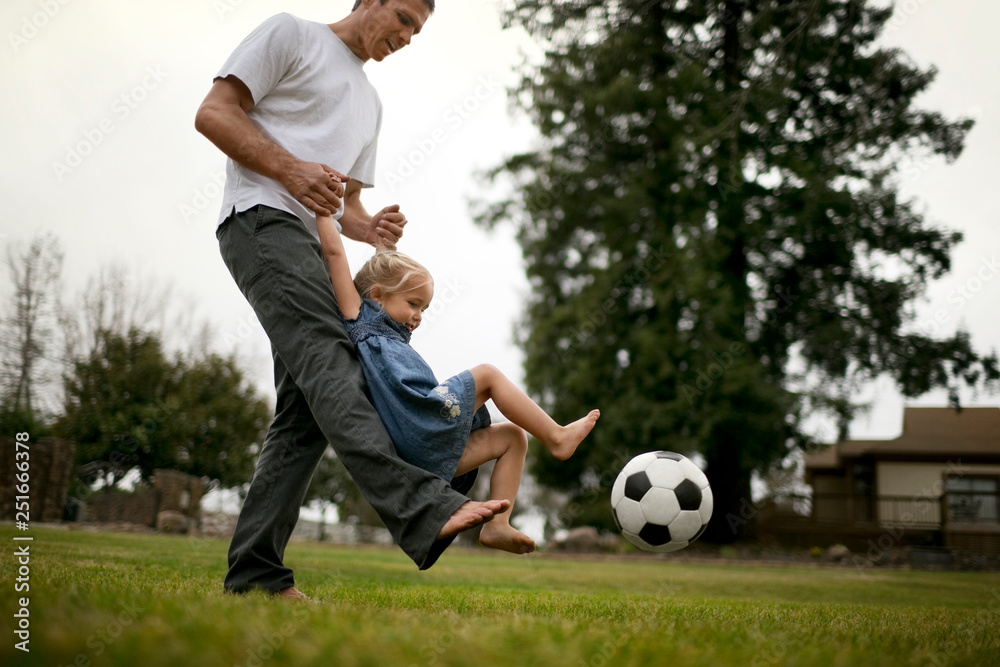 Smiling father teaches his little girl how to kick a soccer ball on the ...