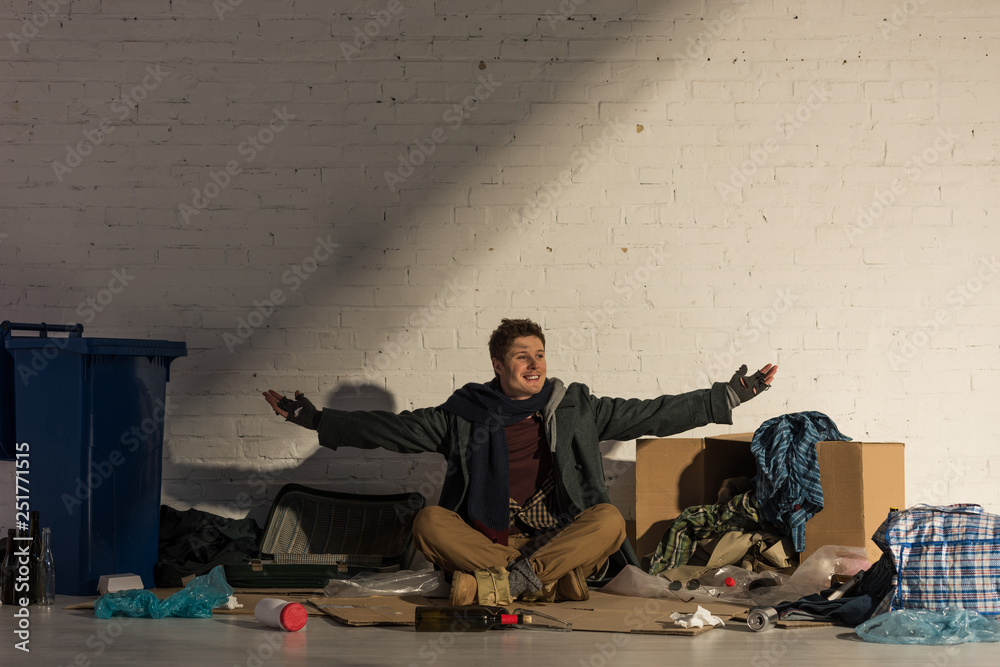 smiling homeless man sitting on cardboard surrounded by rubbish and ...