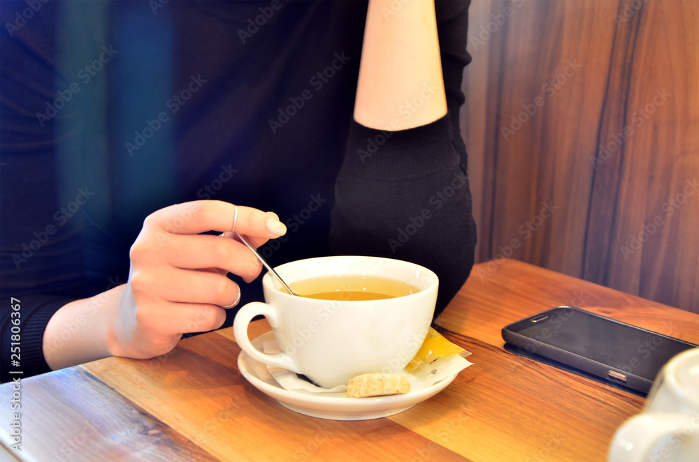 A young girl in a café is drinking tea while checking the messages on ...