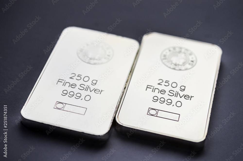 Two minted silver bars weighing 250 grams each on a dark background ...