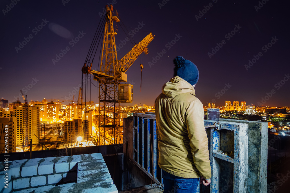 Builder on rooftop of unfinished modern building on crane and ...