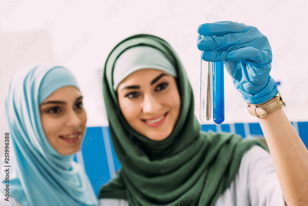 smiling female muslim scientists holding glass test tubes with reagents ...