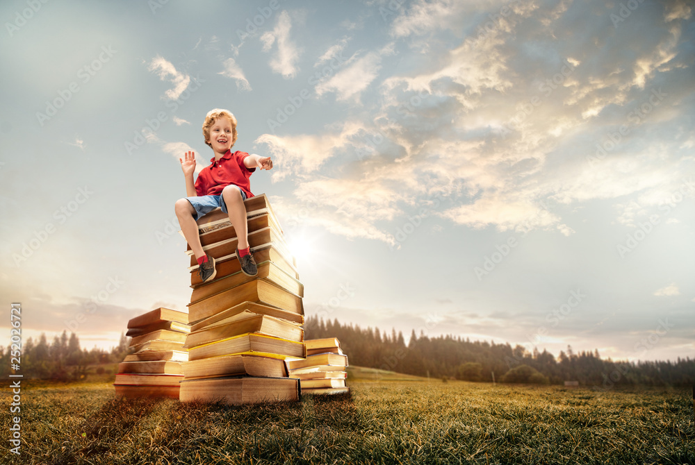 Little boy sitting on the tower made of big books. Childhood dreams ...