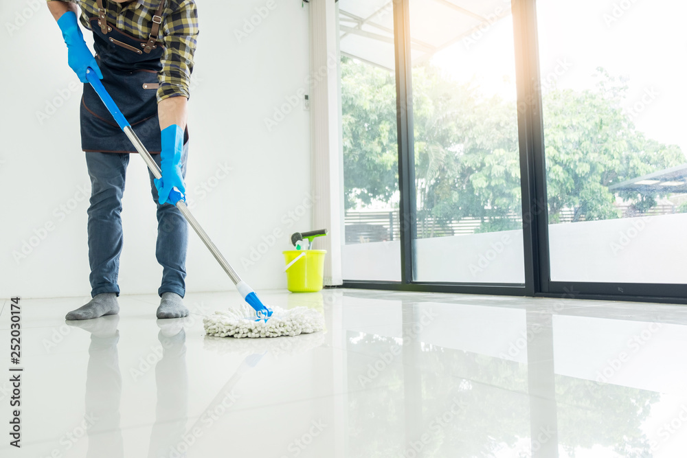 Young housekeeper cleaning floor mobbing holding mop and plastic bucket ...