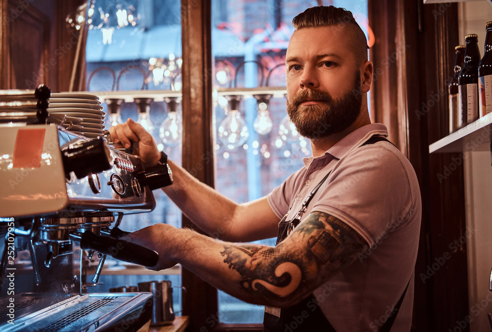 Handsome tattooed barista with stylish beard and hairstyle working on a ...