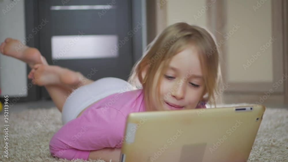 Happy little girl playing with tablet pc computer lying on floor at ...