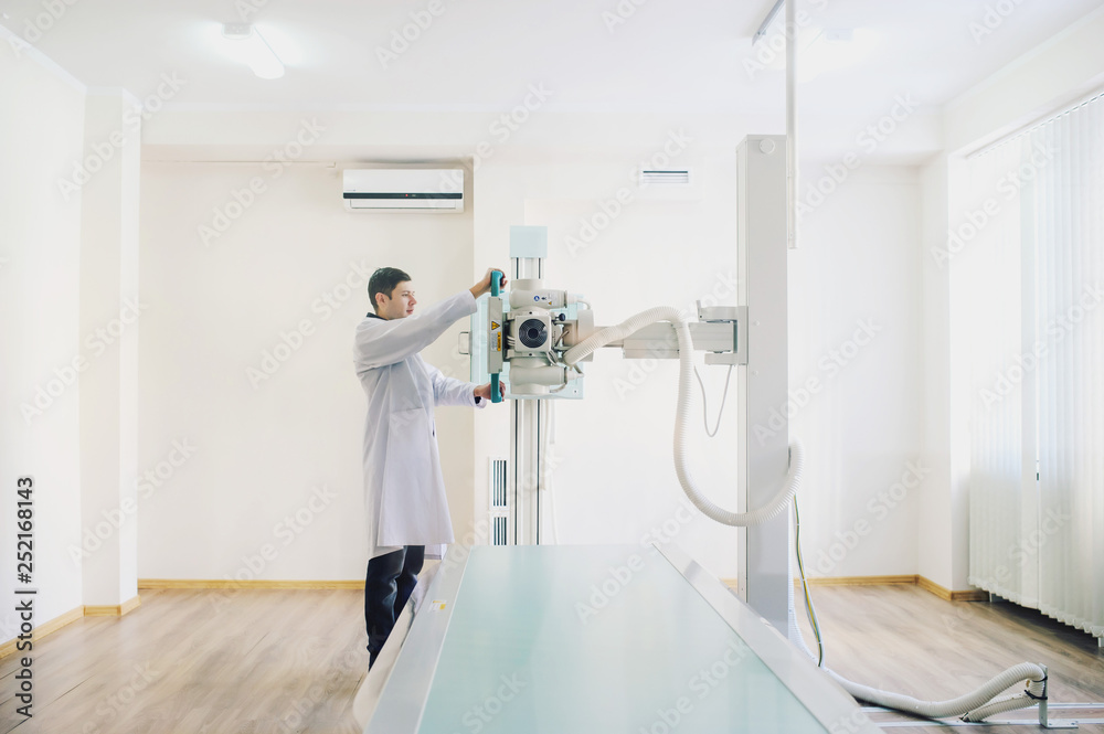 lateral view of a male radiologist adjusting the X-ray machine in ...
