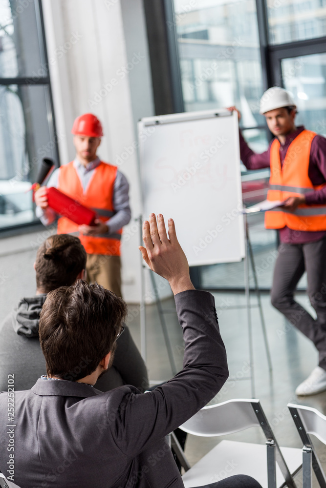Selective focus of man raising hand near handsome firemen in helmets ...