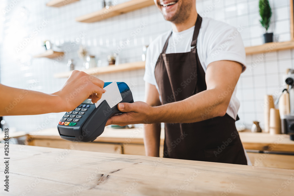 cropped view of cashier standing near bar counter and holding terminal ...