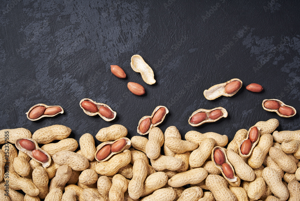 Shelled and unshelled peanut on black table, with copy space. Top view ...