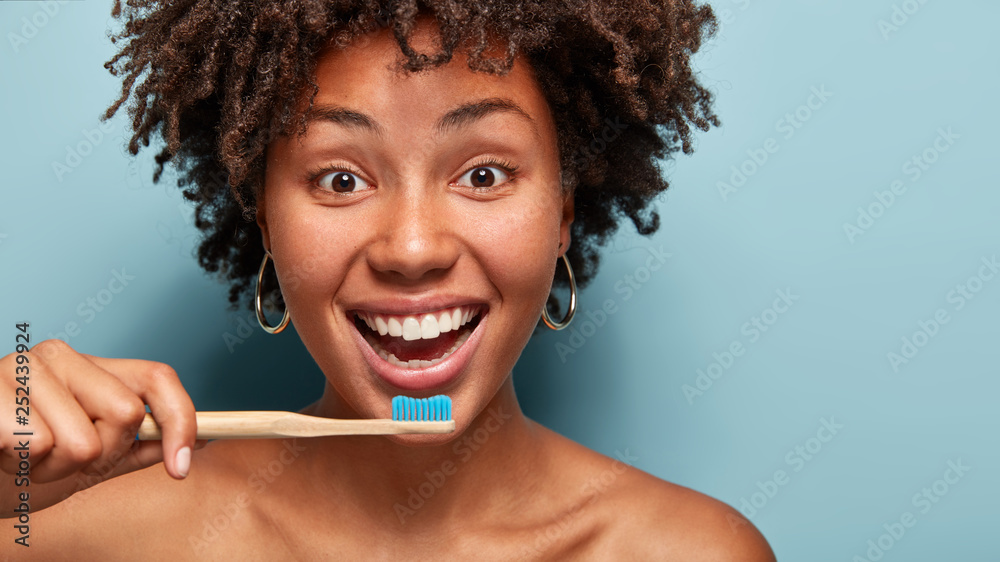 Studio shot of cheerful dark skinned beautiful woman holds toothbrush ...