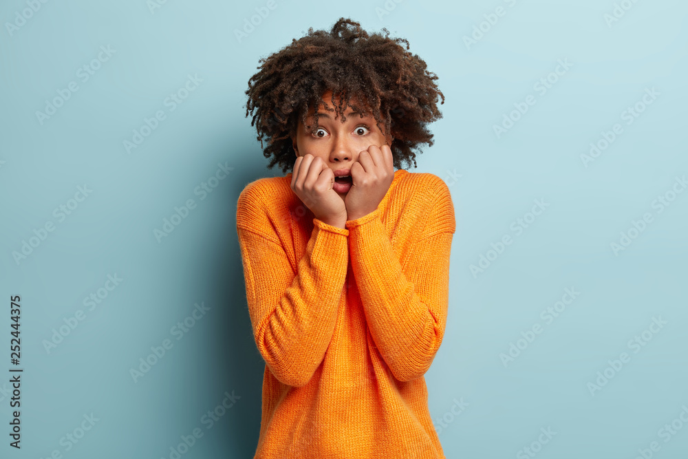 Concerned black young woman shakes from fear, keeps hands near mouth ...