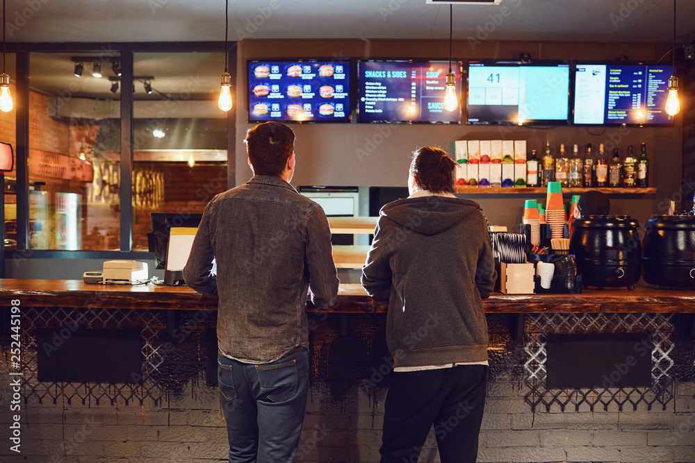 Two men choose food in a fast food restaurant. Stock Photo | Adobe Stock