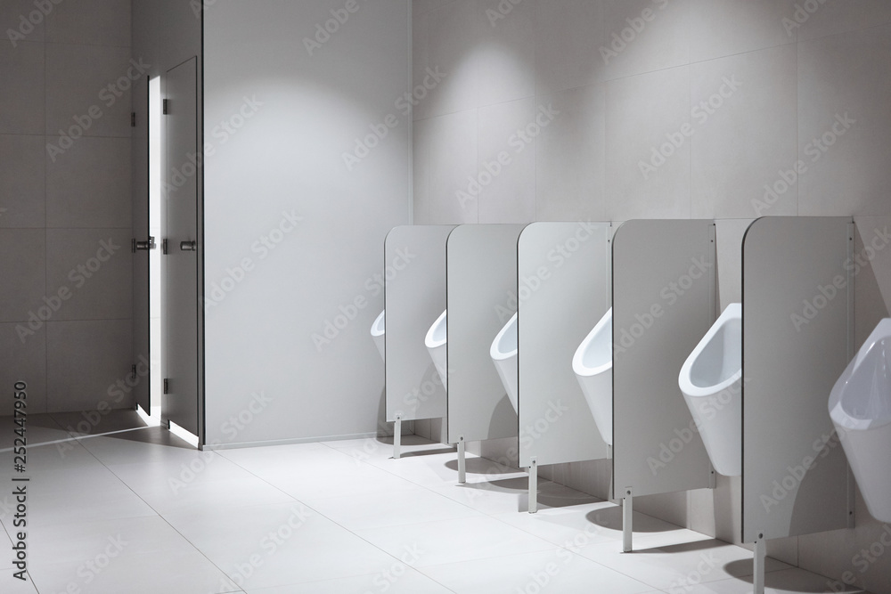 Row of clean porcelain sensor-operated male urinals with partitions in ...