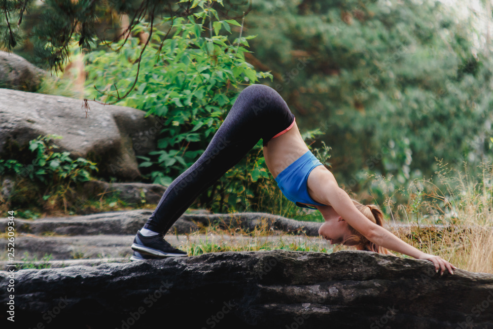 Blonde woman in dog pose downward facing outdoors on a rock in the ...