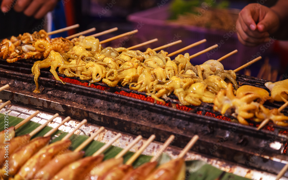 Traditional Asian Thai street food and fast food, delicious grilled squid calamari skewers in ...