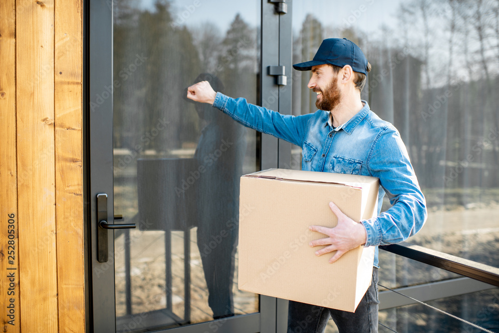 Delivery man knocking door of the modern house, delivering some goods ...