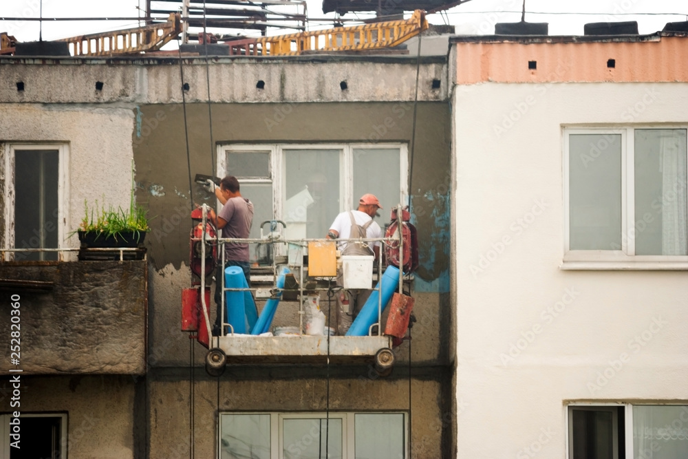 Two workers are plastering the facade of a building without observing ...