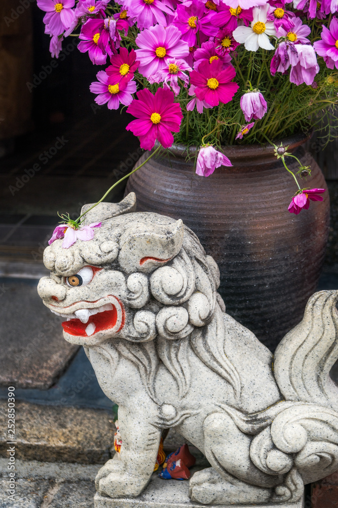 Small lion-dog stone statue in front of a large vase with flowers. Lion ...