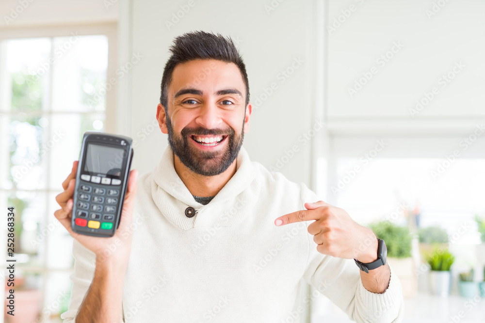 Handsome hispanic man holding point of sale terminal dataphone with ...