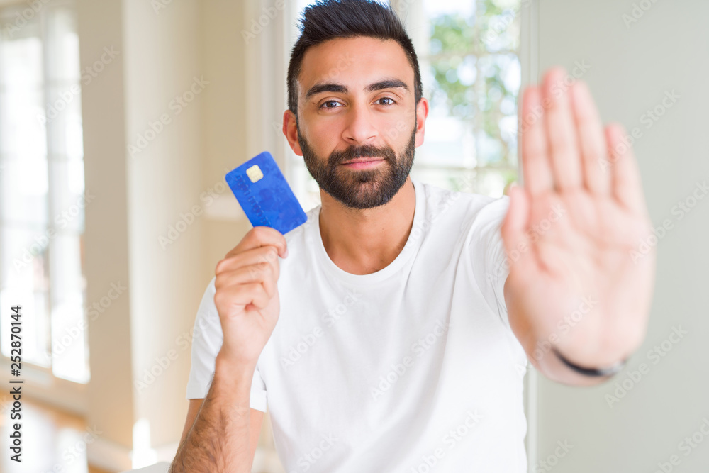 Handsome hispanic man holding credit card with open hand doing stop ...