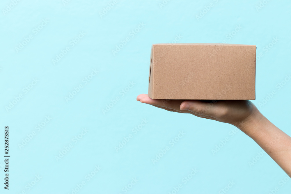 Woman hand hold the brown corrugated box on blue wall background with ...