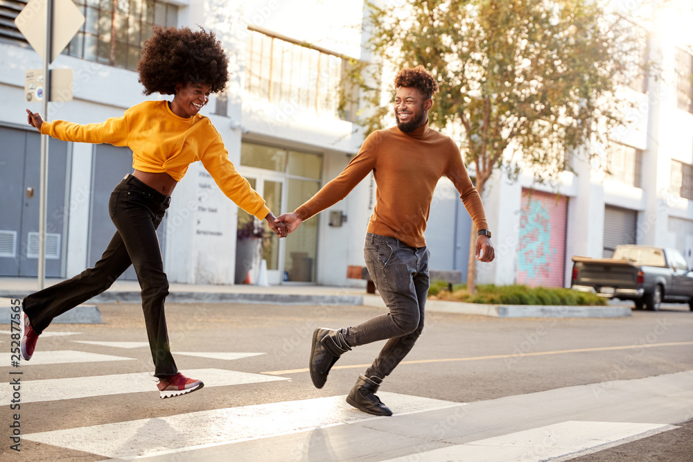 Fashionable young black couple running across a city street holding ...