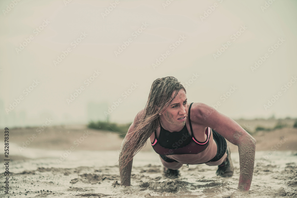 Closeup of strong athletic woman crawling in wet muddy puddle with mud ...